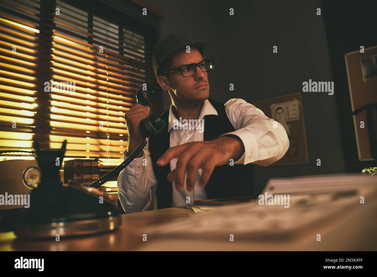 Old fashioned detective dialing telephone number at table in office ...