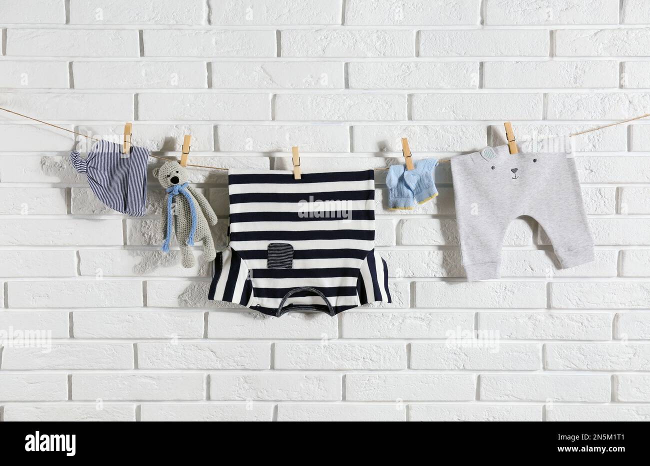 Baby clothes hanging on washing line near white brick wall Stock Photo ...
