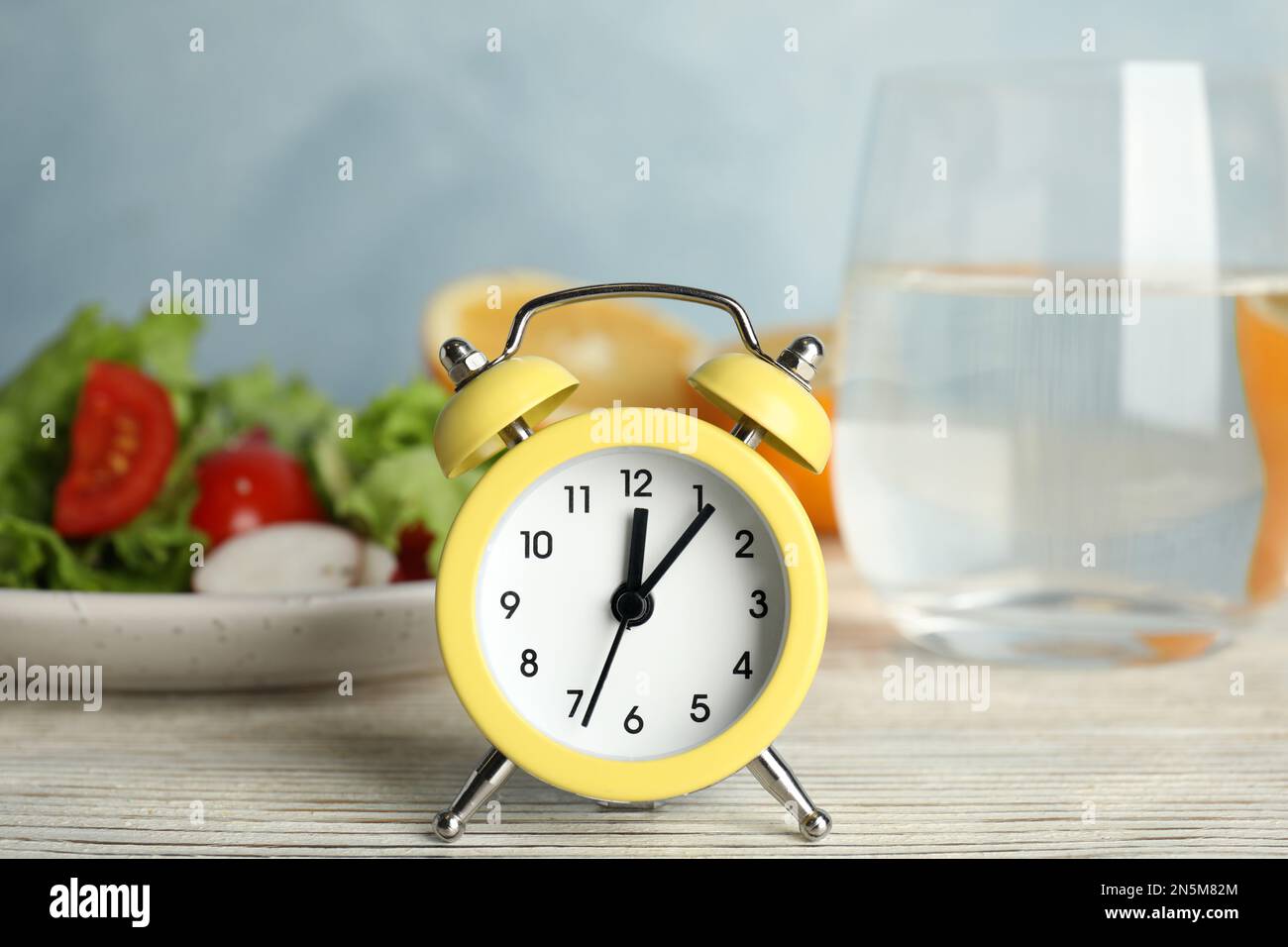 Alarm clock and healthy food on white wooden table. Meal timing concept ...
