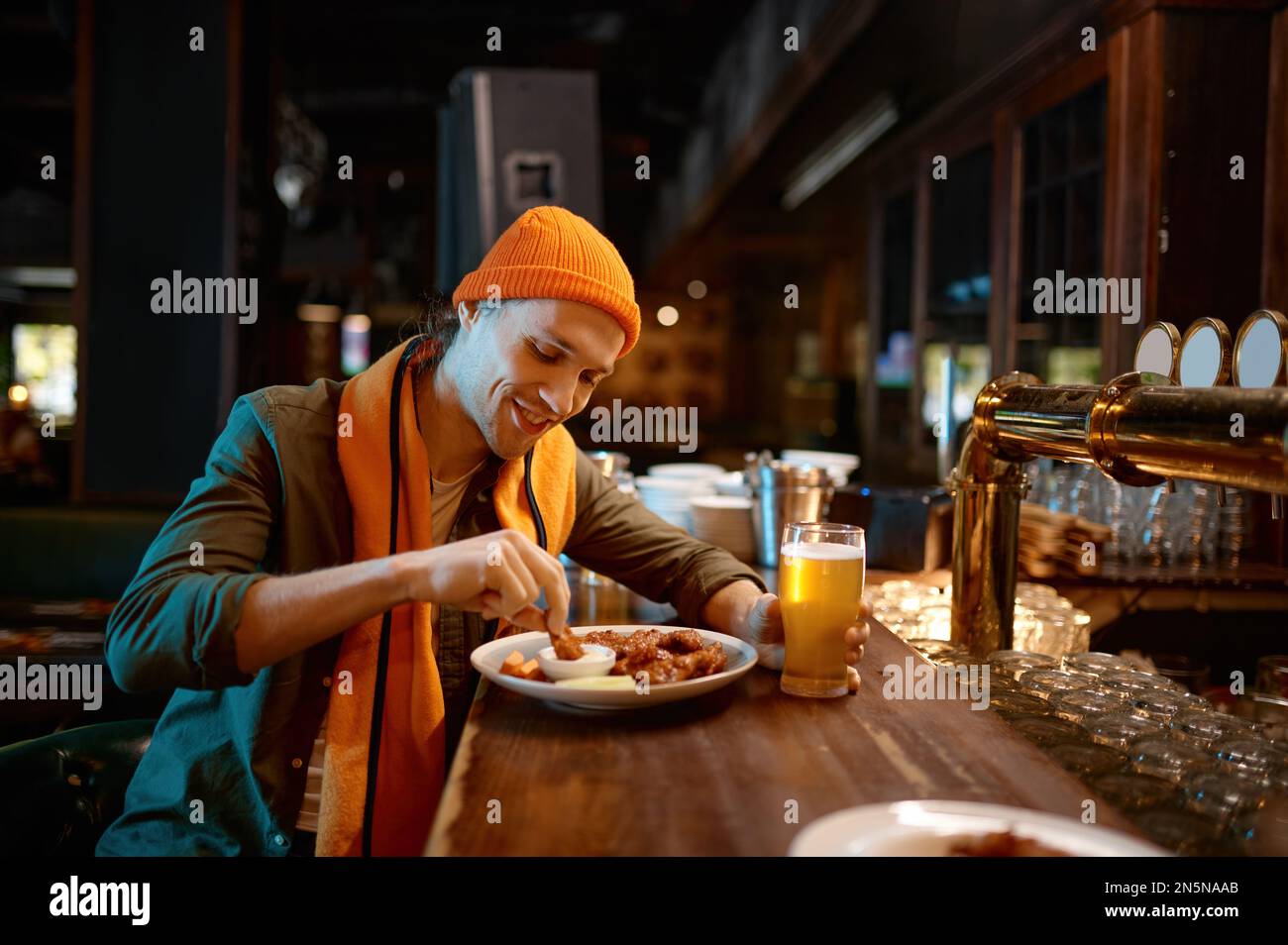 Young man football fan eating snack and drinking beer in sports bar ...