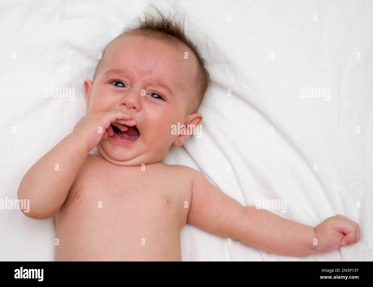 Crying baby lies on a white fluffy background Stock Photo - Alamy