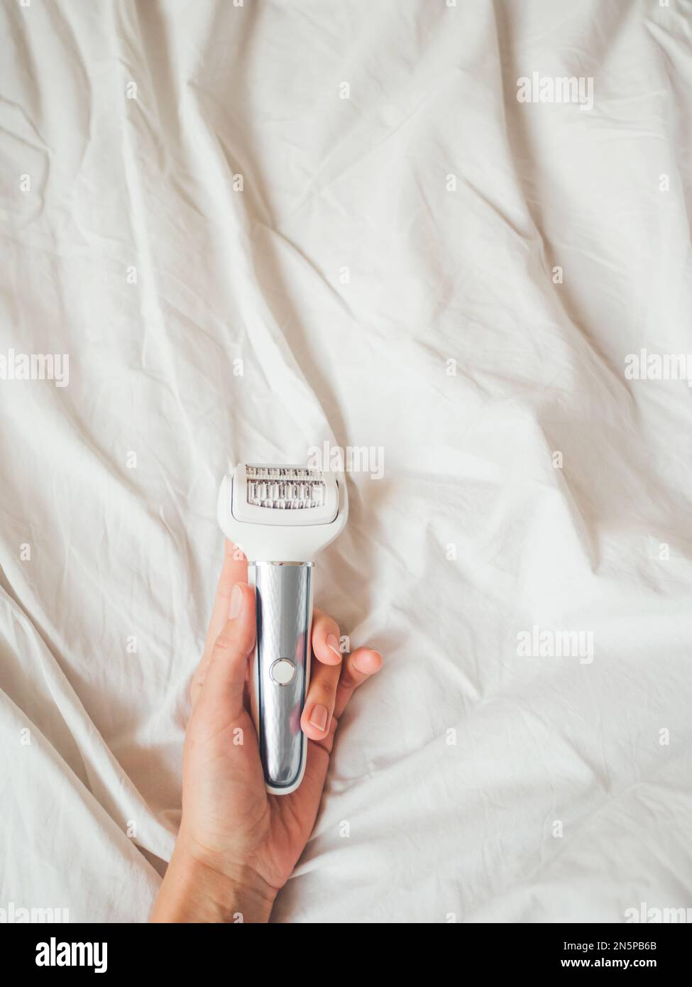 Woman holds epilator on crumpled bed background. Epilation ...