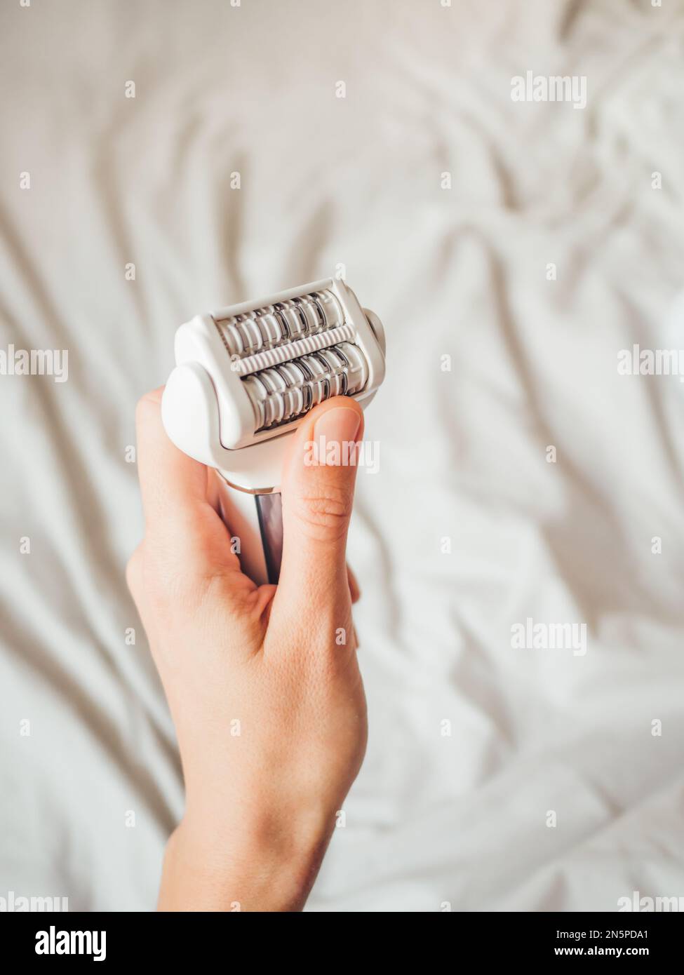 Woman holds epilator on crumpled bed background. Epilation ...