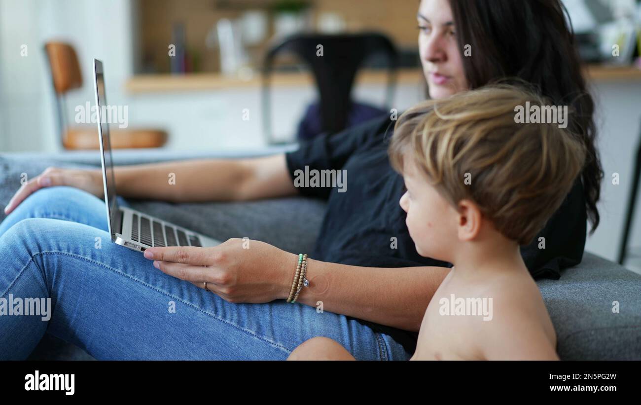 Mother parenting with child in front of laptop screen working from home ...