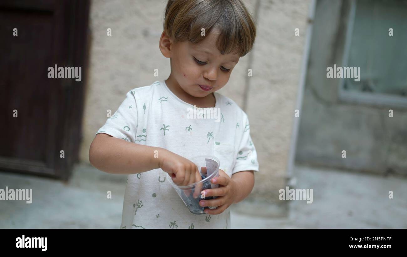 One little boy eating blueberries. Child standing outside snacking ...