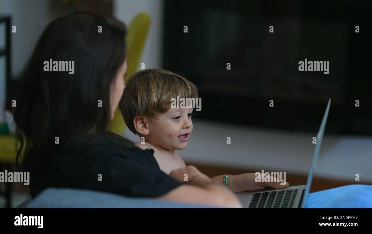 Mother and child in front of laptop at home sofa. Parent working with ...
