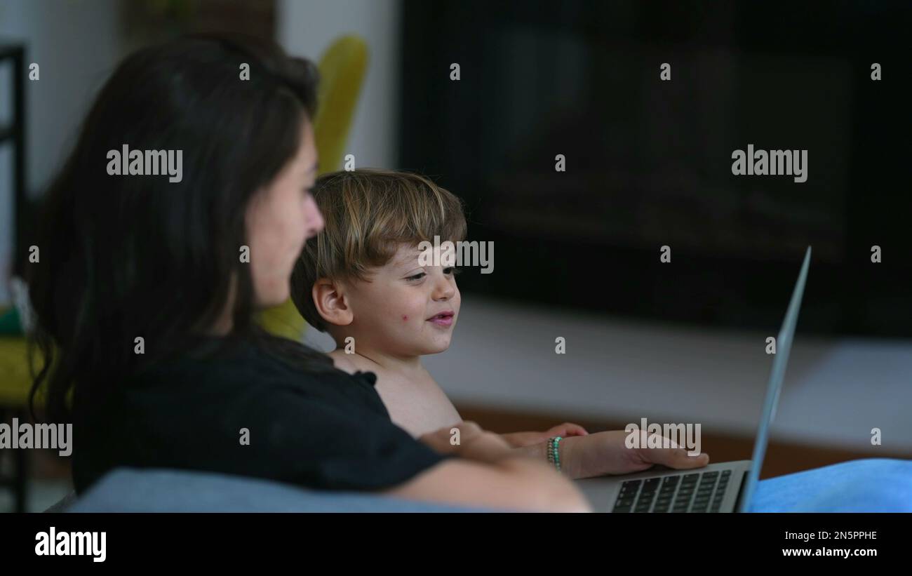 Mother and child in front of laptop at home sofa. Parent working with ...