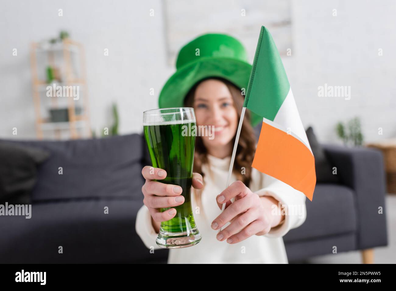 Blurred woman in hat holding green beer and Irish flag at home Stock ...