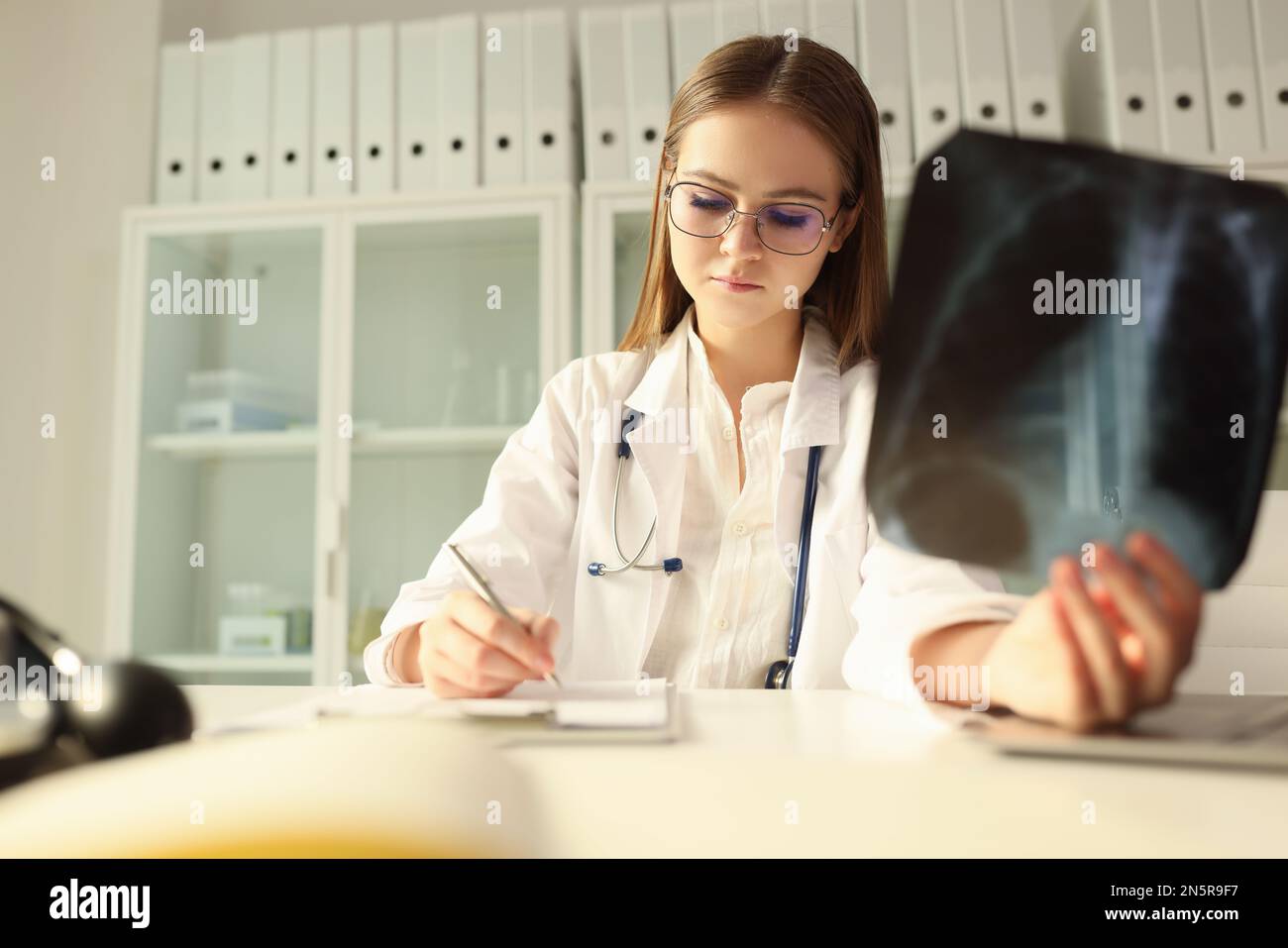Young doctor in glasses checks x-ray scans and makes notes in medical ...