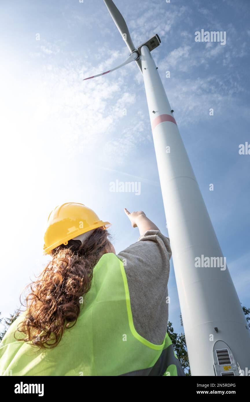 Female engineer with brown curly hair and yellow helmet is pointing at ...