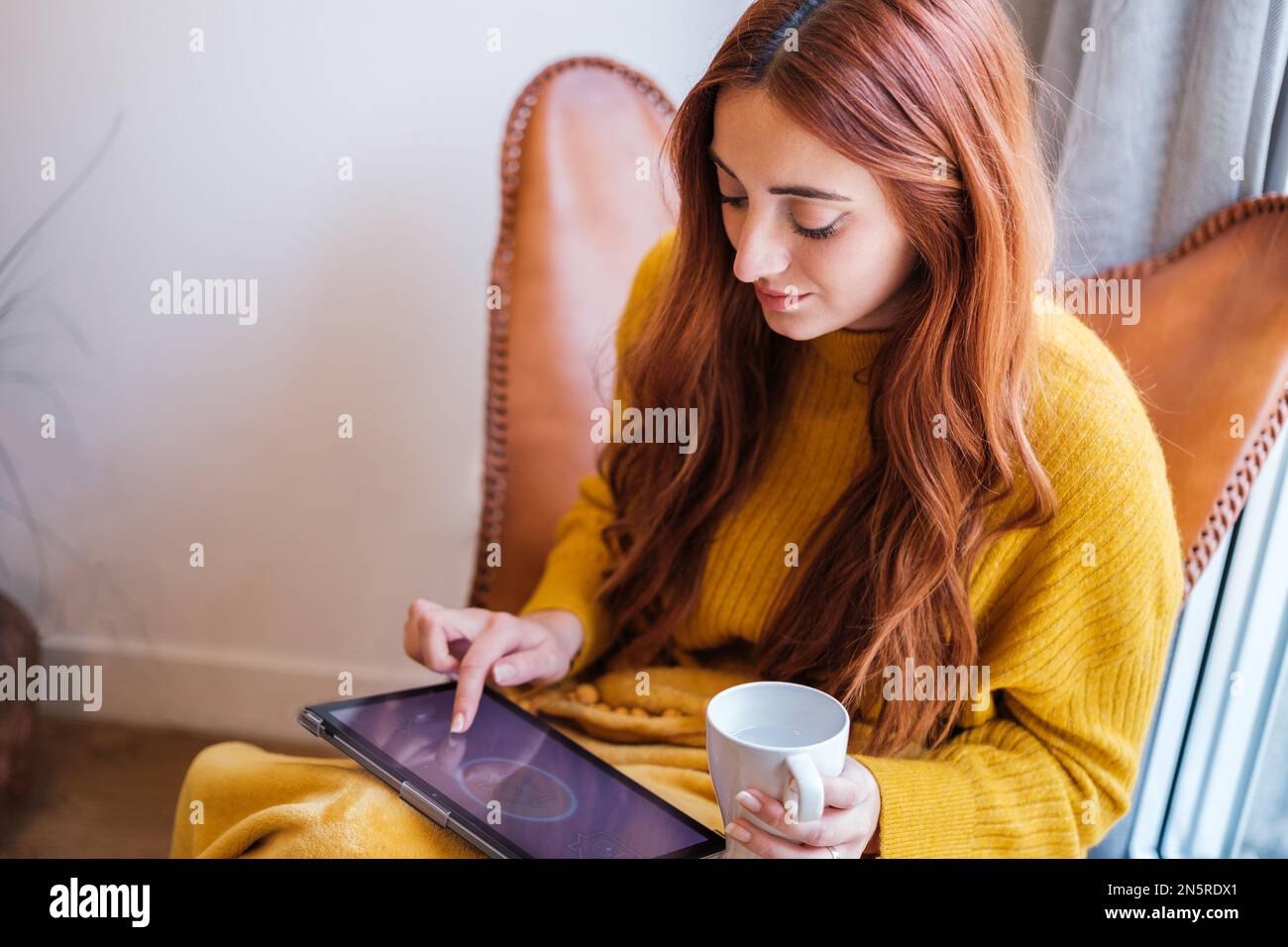 Young redhead woman managing the different technologies of the house from the home app. Concept ...