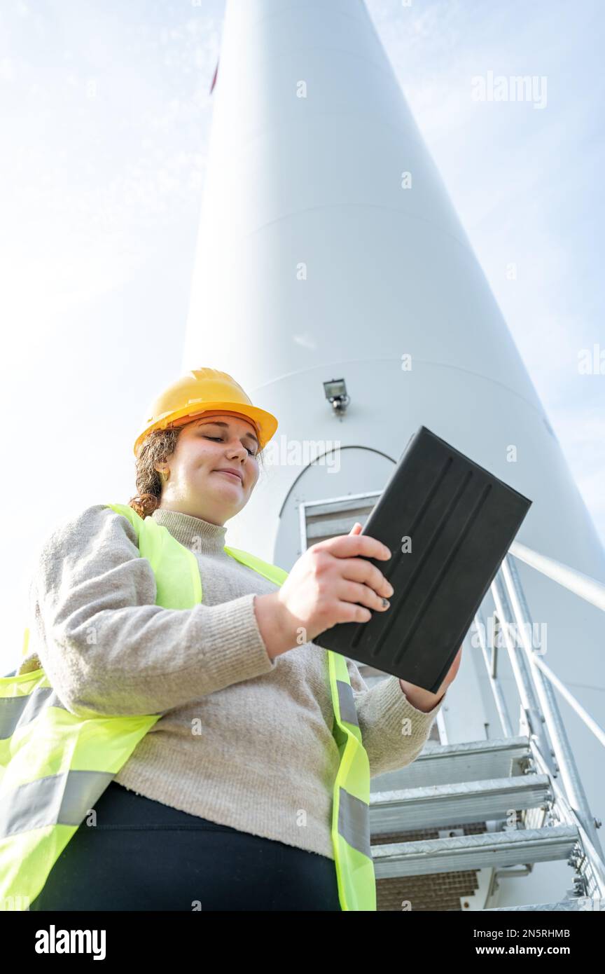 Female engineer with brown curly hair and yellow helmet is smiling ...