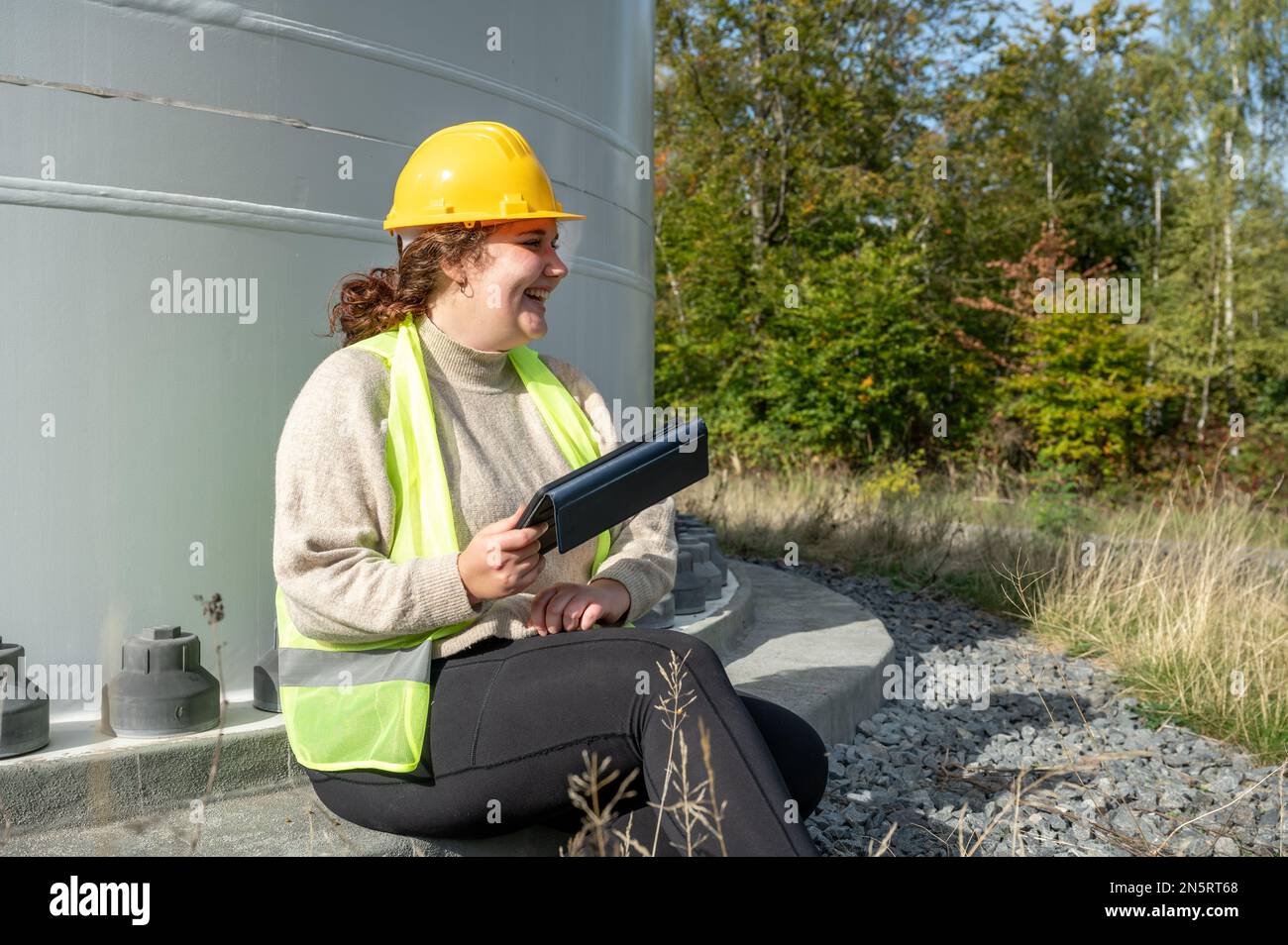 Female engineer with brown curly hair and yellow helmet is smiling and ...