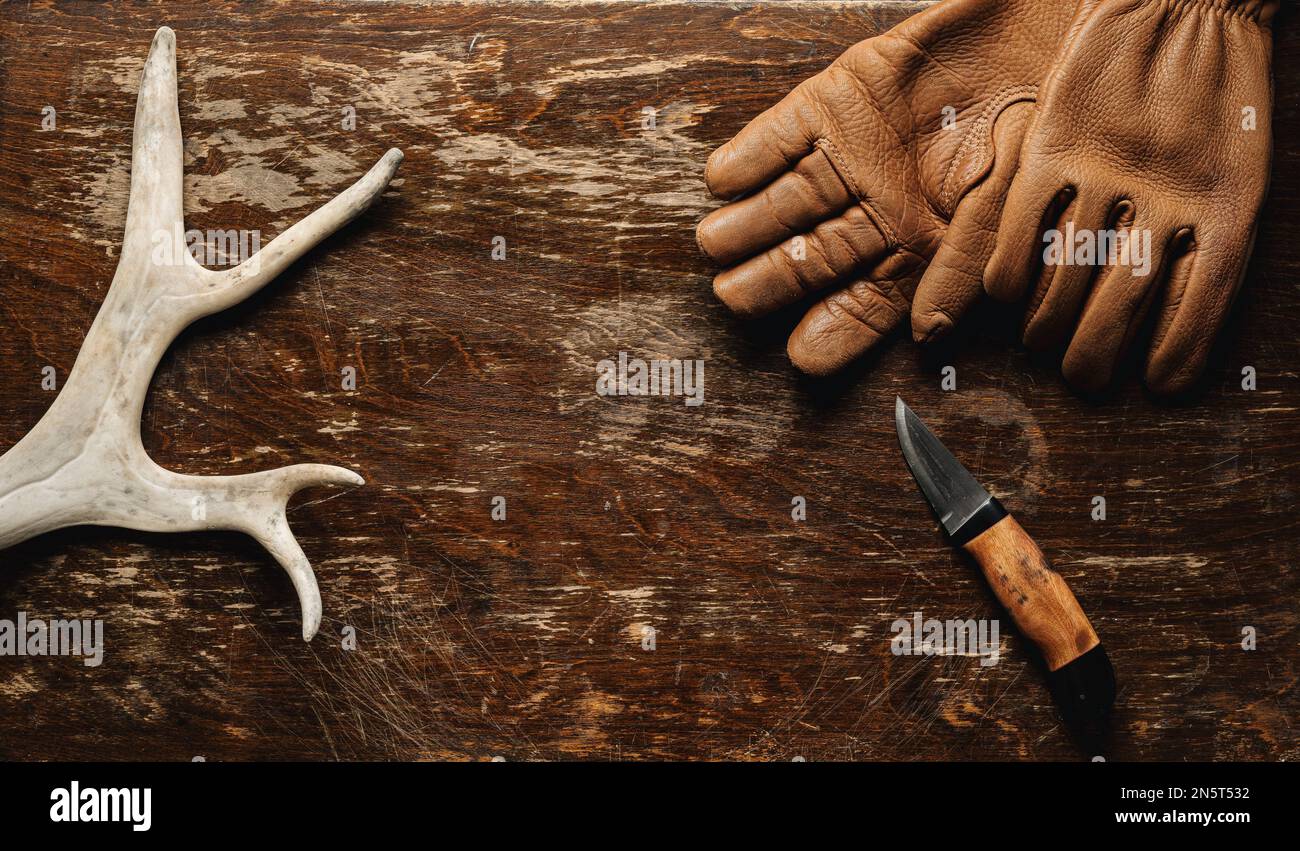 Reindeer antlers, leather gloves and a hunting knife on a rustic wooden ...