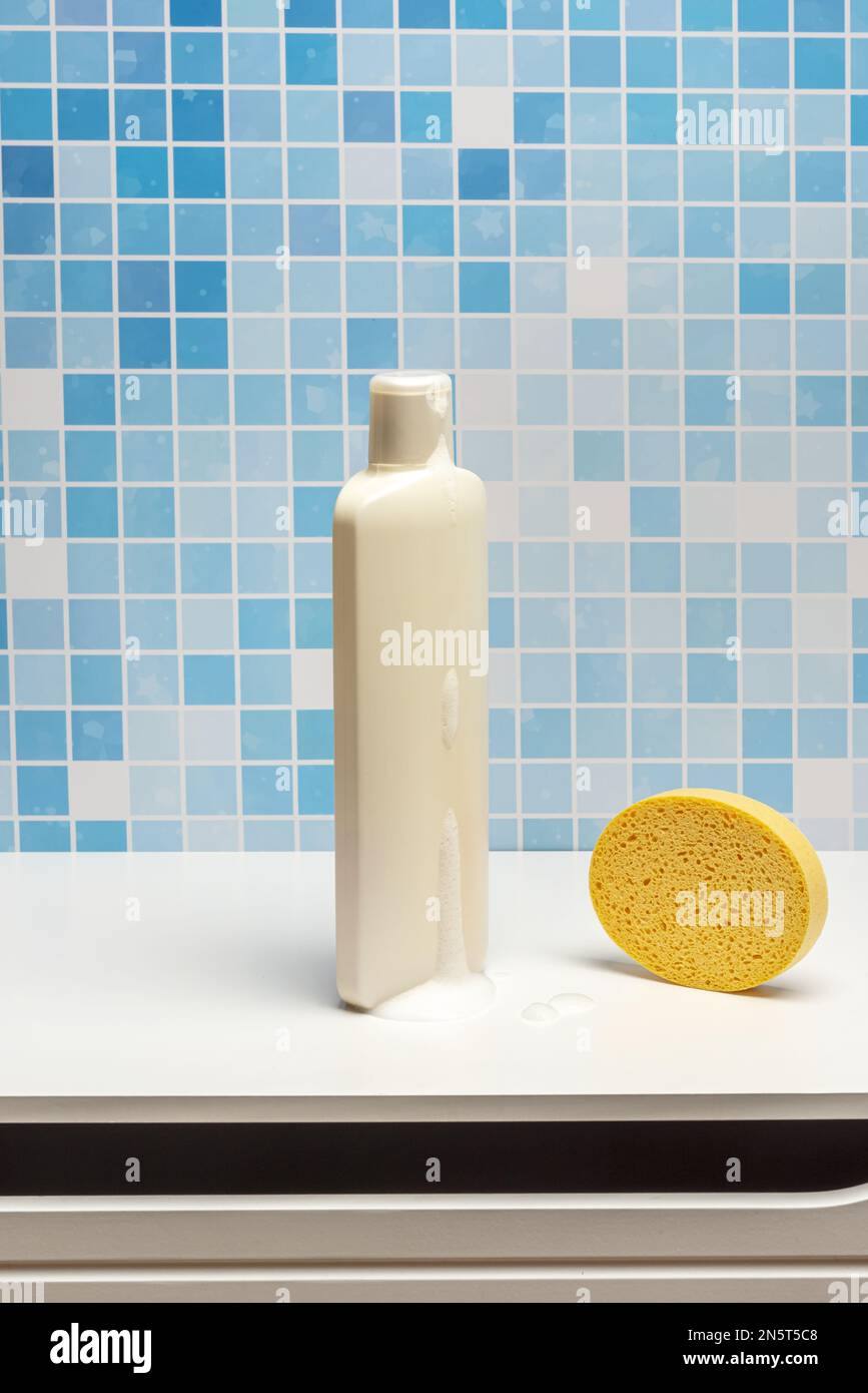 A bottle of shampoo with foam and a yellow sponge on a white surface in ...