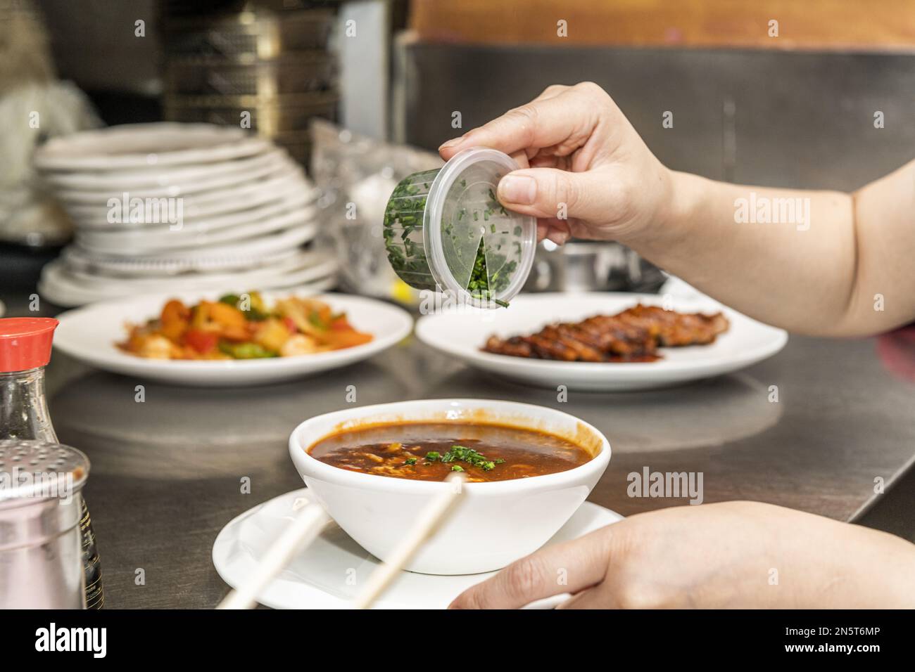 A Chinese restaurant waitress garnishing a soup with chives in a white ...