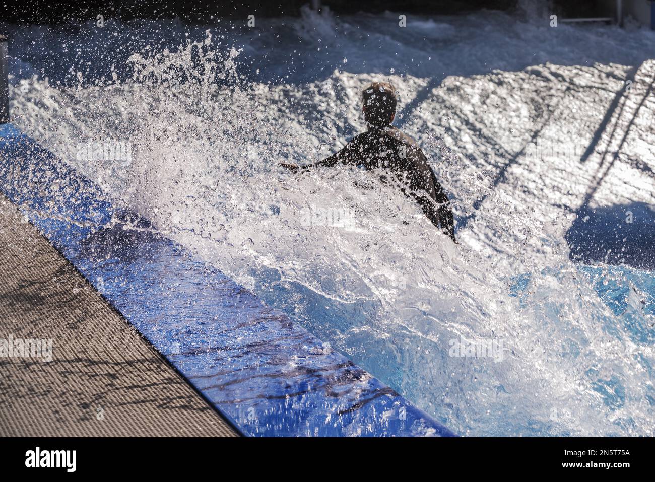 A surfer in the water giving it a go in a wave pool with big splashes ...