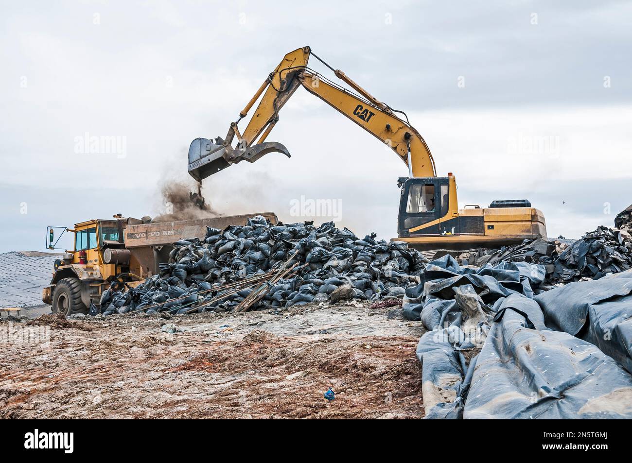 A power shovel loads debris onto a a dump truck in an active landfill ...