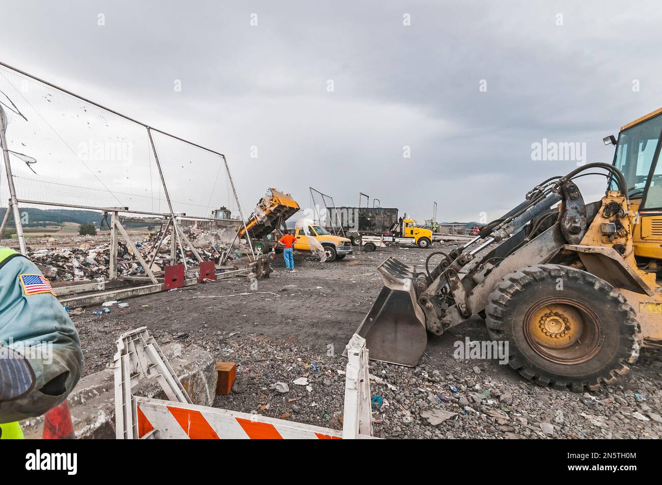 A worker's sleeve, Caterpillar loader in the foreground, with a dump ...