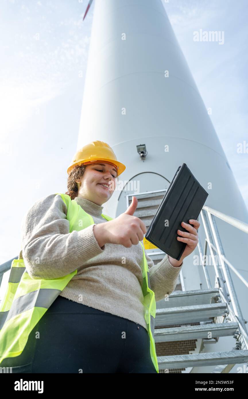 Female engineer with brown curly hair and yellow hat is giving a thumbs ...