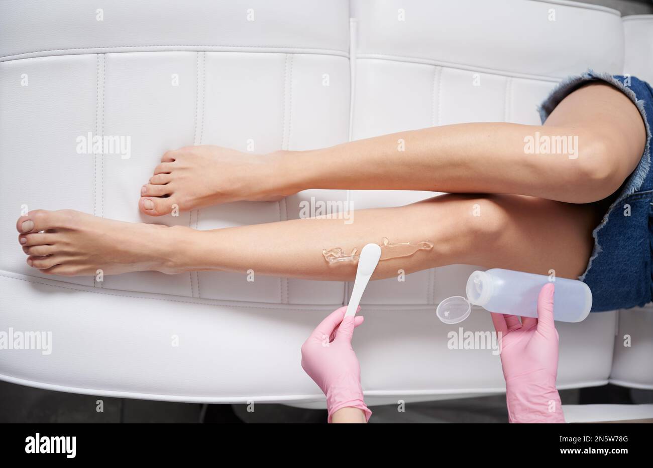 Beautician's hands applying special gel for epilation on client's feets ...