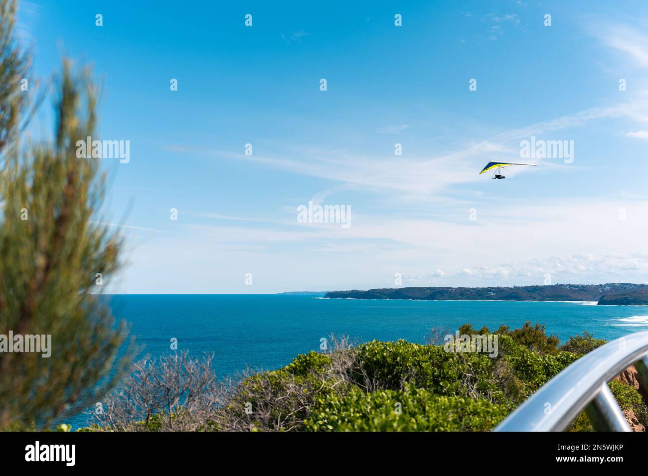 A hang glider soaring over a tranquil azure sea on a clear, sunny ...