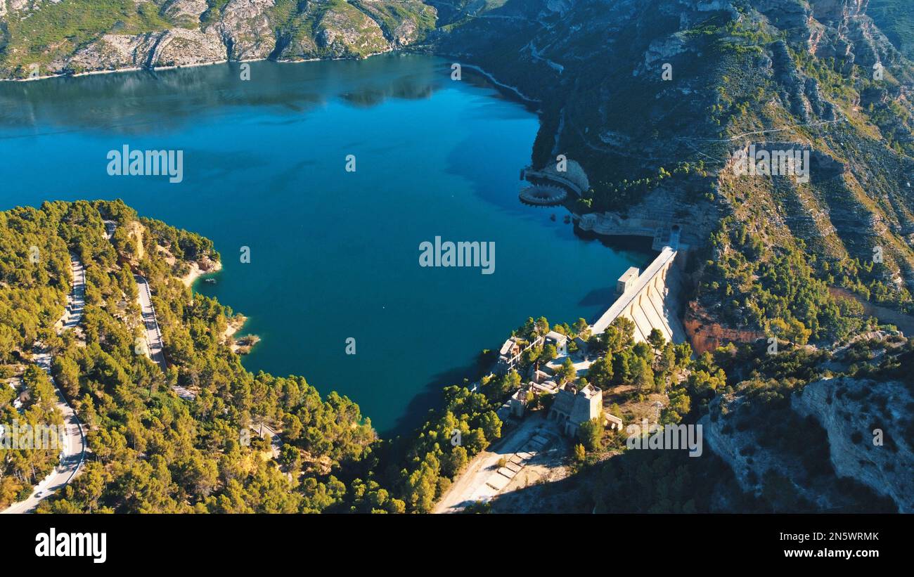 An aerial of a turquoise dam surrounded by beautiful mounts covered in ...