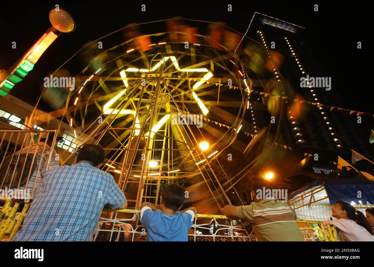 Filipinos watch a ferris wheel at a city funfair during the Christmas ...
