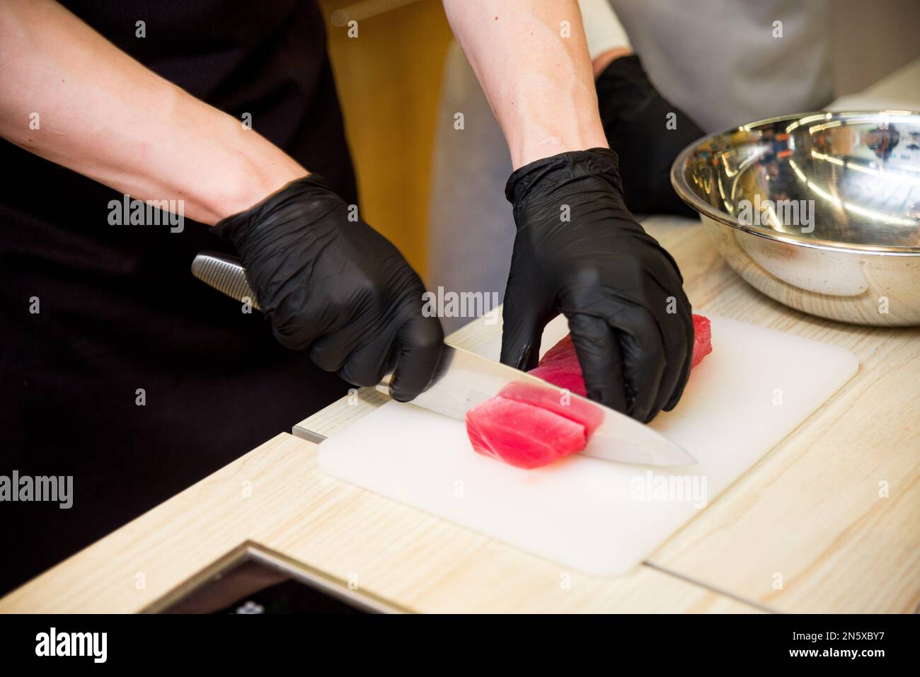 the chef's hands in black gloves cut the raw tuna fillets into slices ...