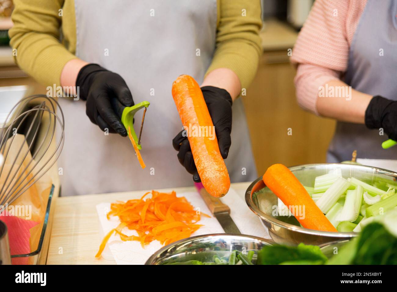 women's hands hold a vegetable peeler and peel carrots, the process of cooking, culinary class ...
