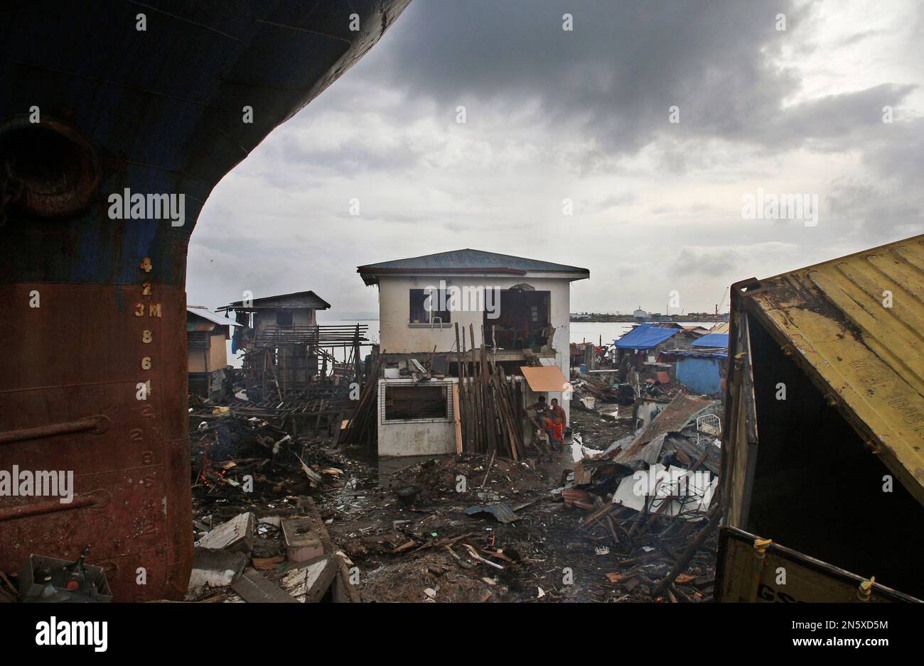 Typhoon survivors gather outside a damaged house near shipping vessels ...