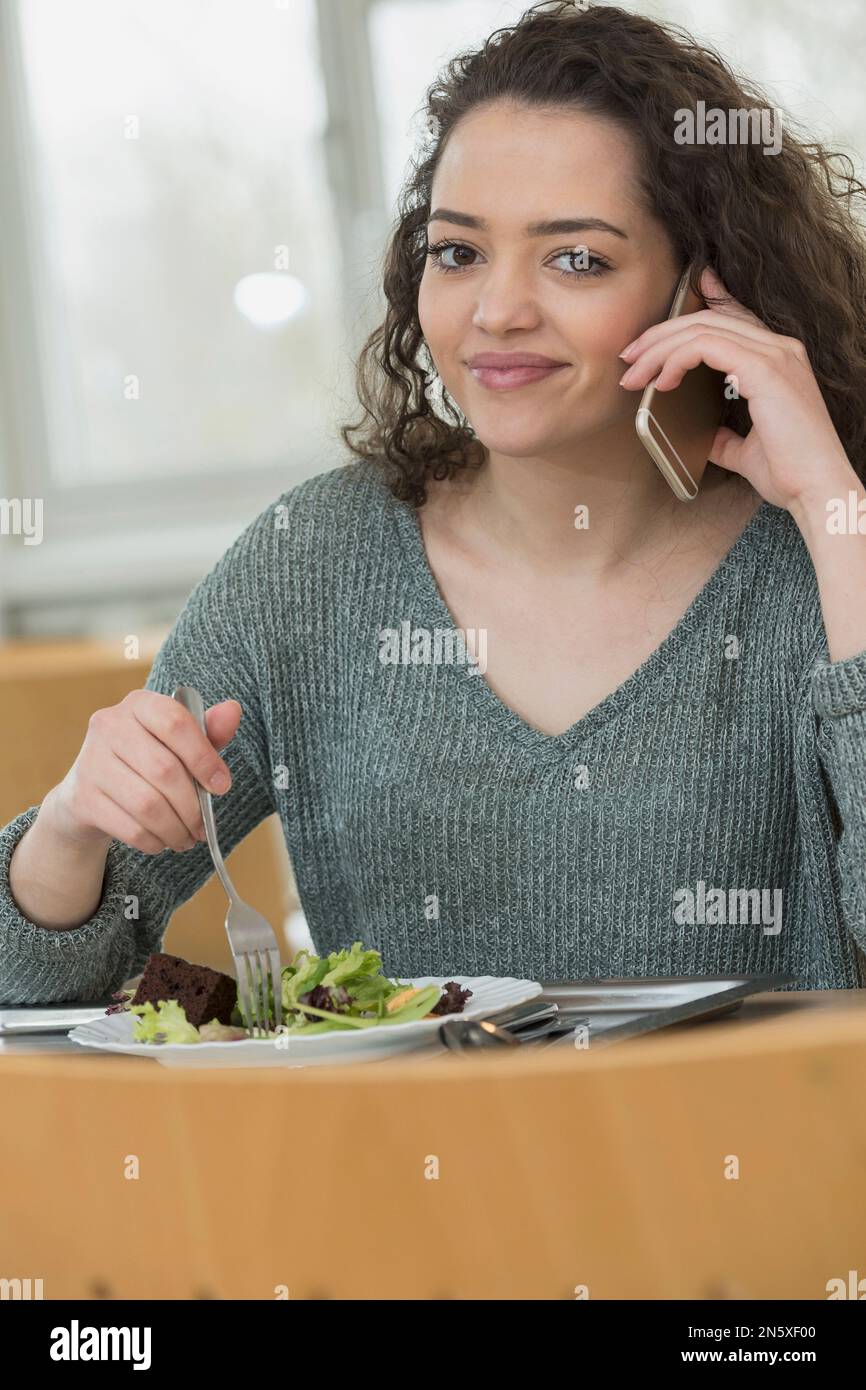 University student eating salad in canteen and talking on mobile phone ...