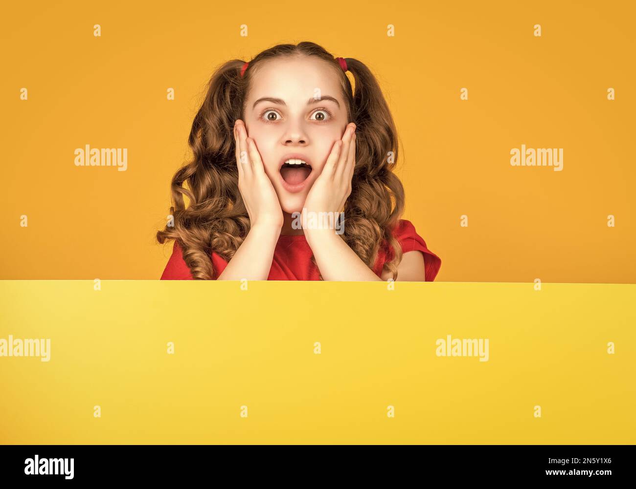 shocked child behind blank yellow paper with copy space for ...