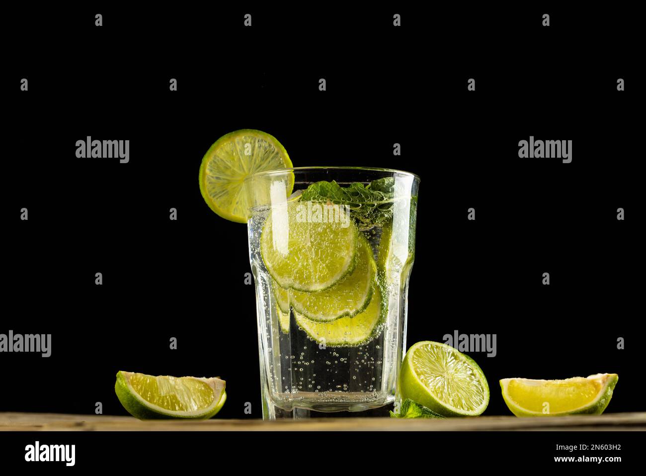 Glass with water and limes on wooden table with copy space over black ...