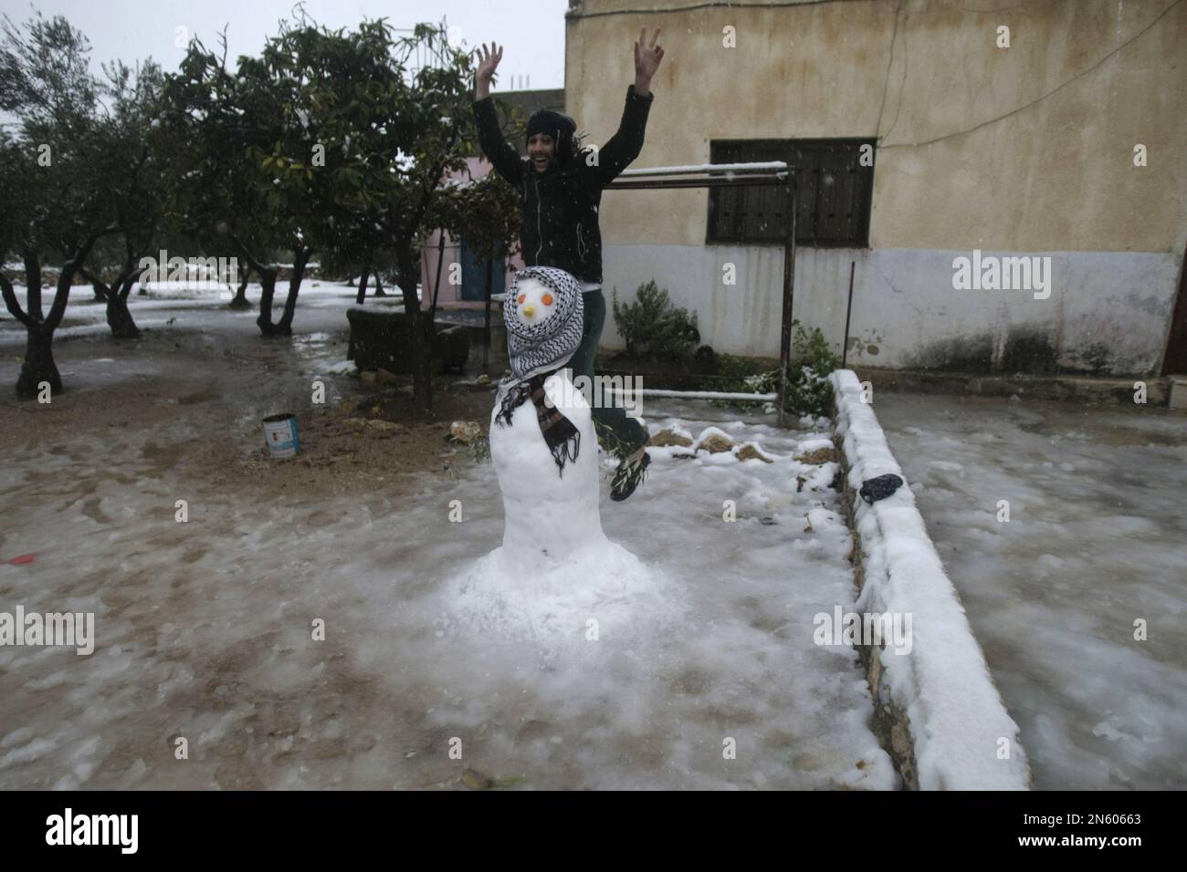 A Palestinian youth jumps next to a snowman he made in the West Bank ...