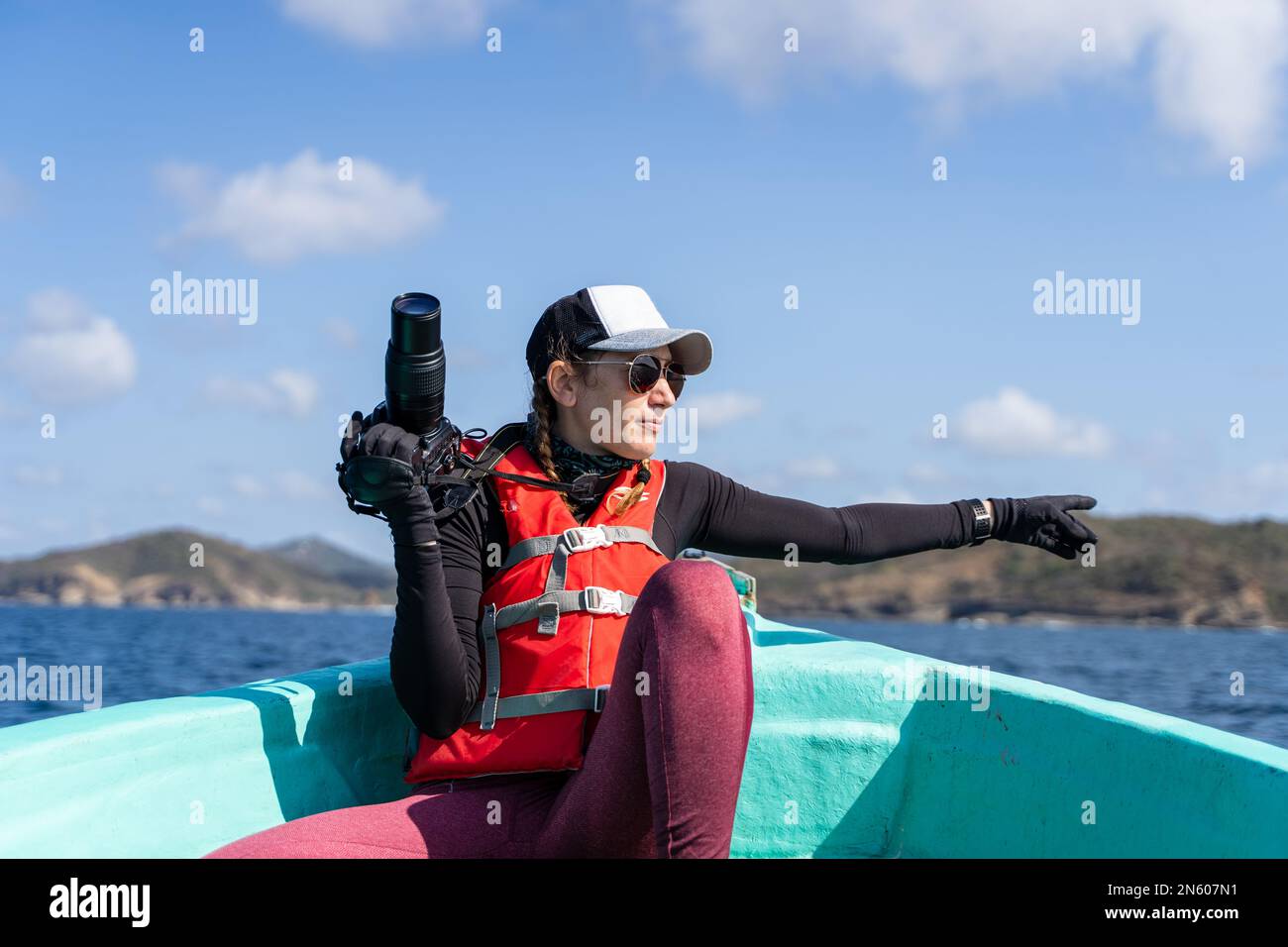Marine biologist pointing to the sea while carrying a camera on a boat ...