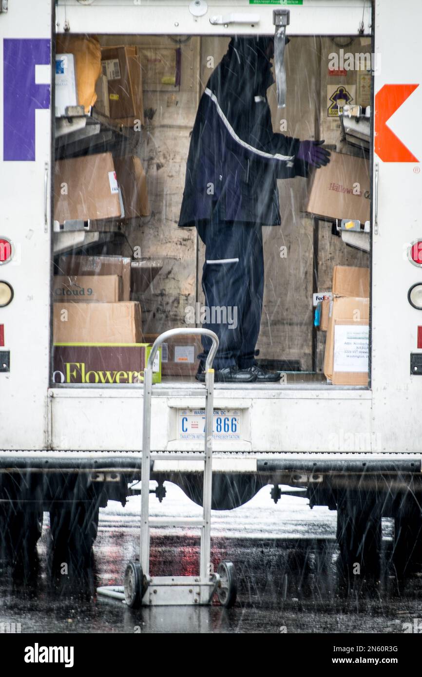 A delivery worker organizes packages in the back of the truck as snow ...