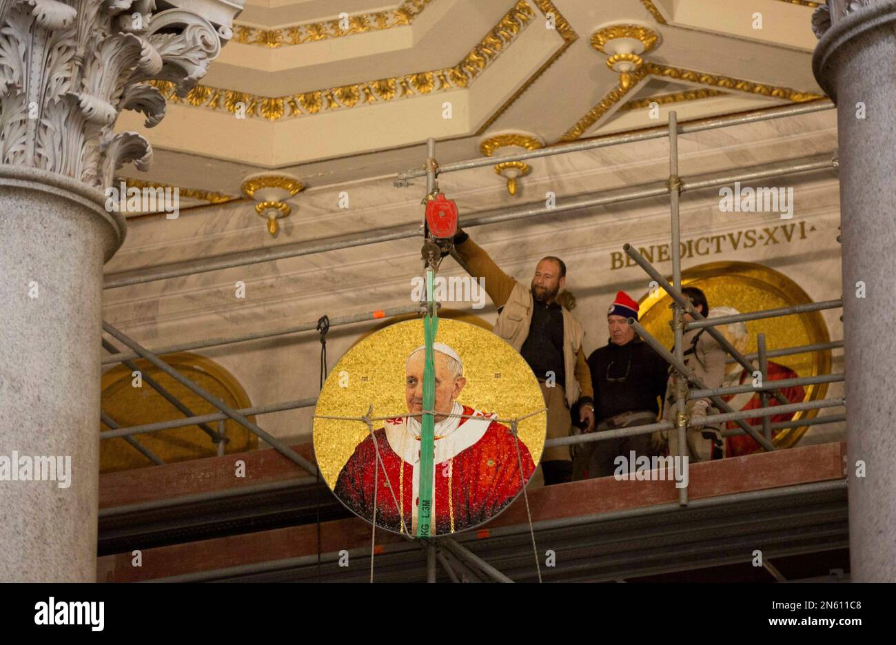 A mosaic icon of Pope Francis is lifted to be placed next to the icon ...