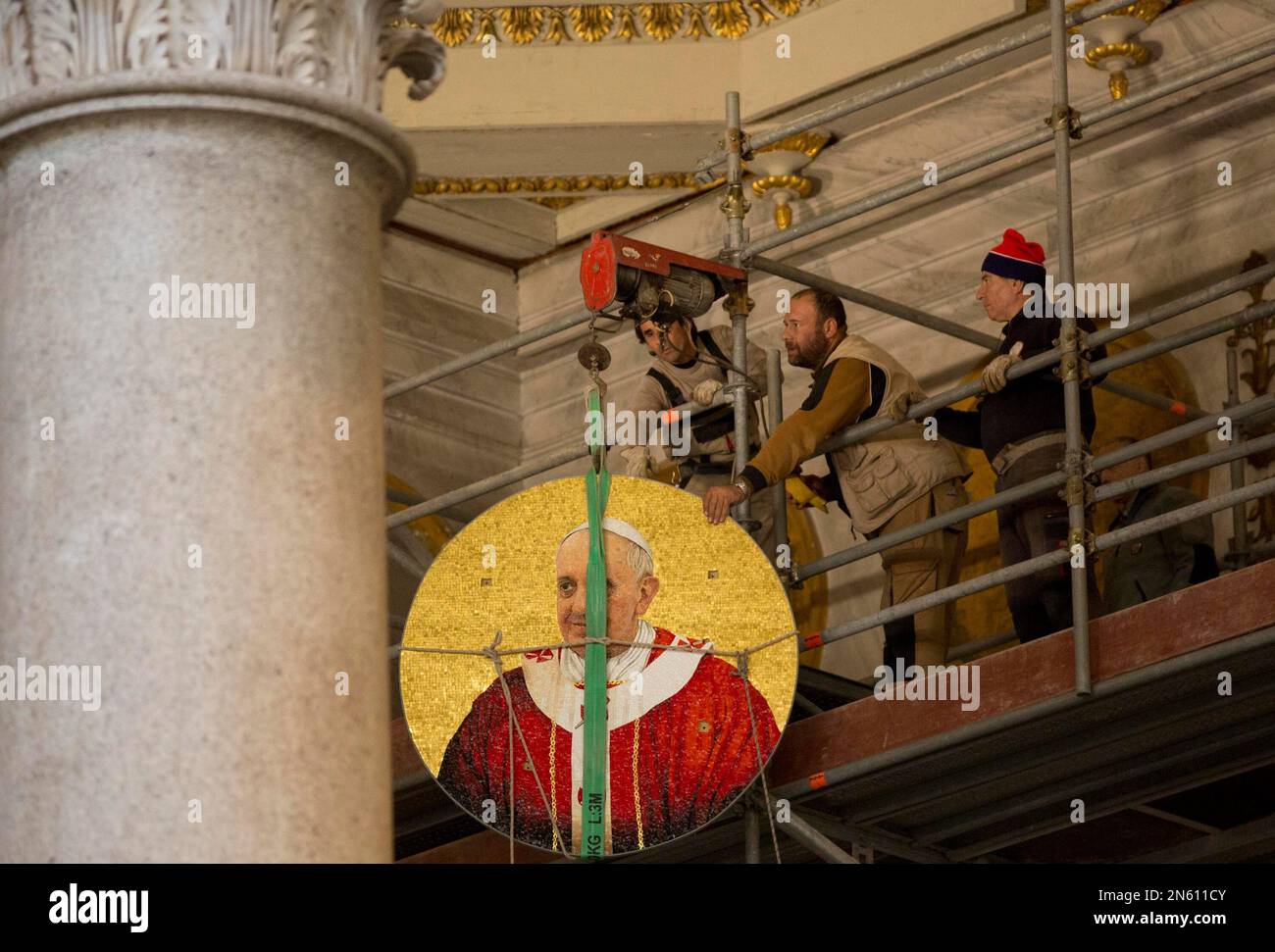 A mosaic icon of Pope Francis is lifted to be placed next to the icon ...