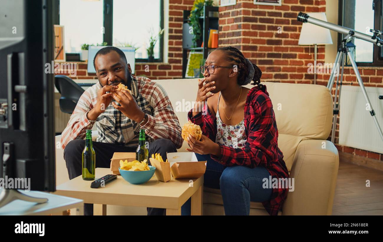 Modern life partners taking bite of cheeseburger, eating fast food from ...
