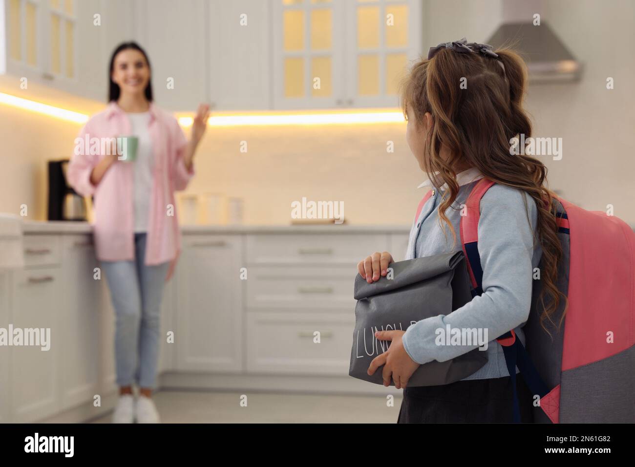 Little girl with lunch bag and mother in kitchen. Getting ready for ...
