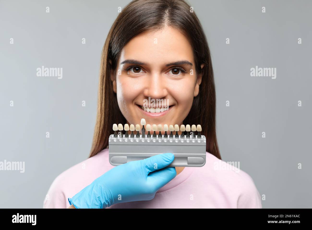 Doctor checking young woman's teeth color on light grey background ...