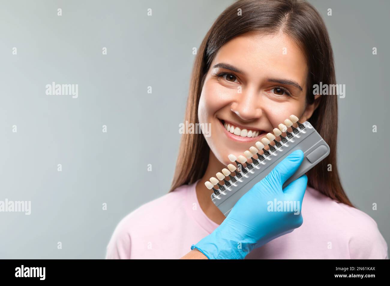 Doctor checking young woman's teeth color on light grey background ...