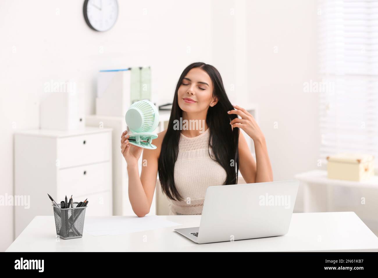 Young woman enjoying air flow from fan at workplace Stock Photo - Alamy