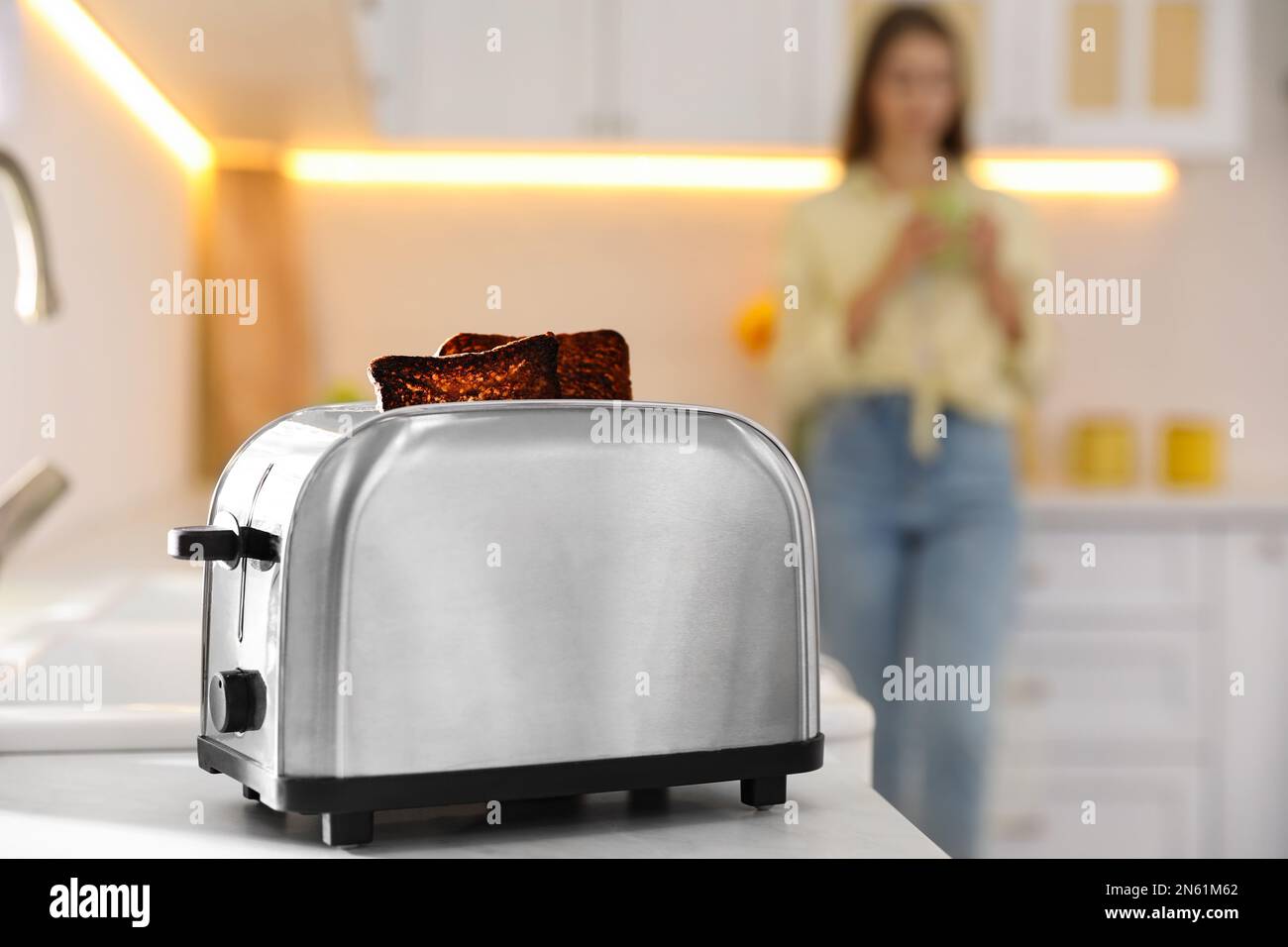 Modern toaster with slices of burnt bread and blurred woman on ...