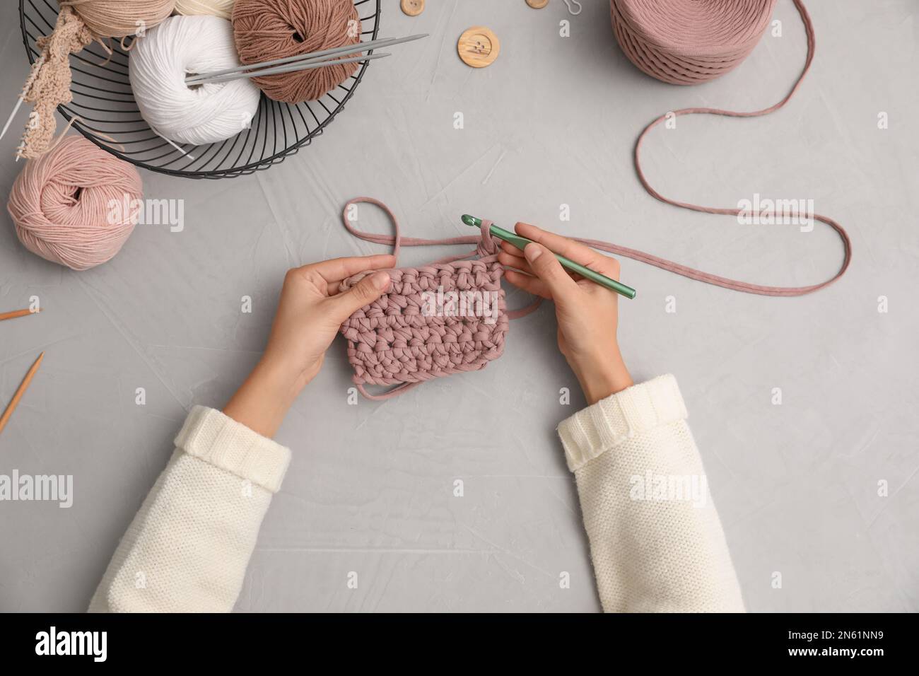 Woman crocheting with threads at grey table, top view. Engaging hobby ...