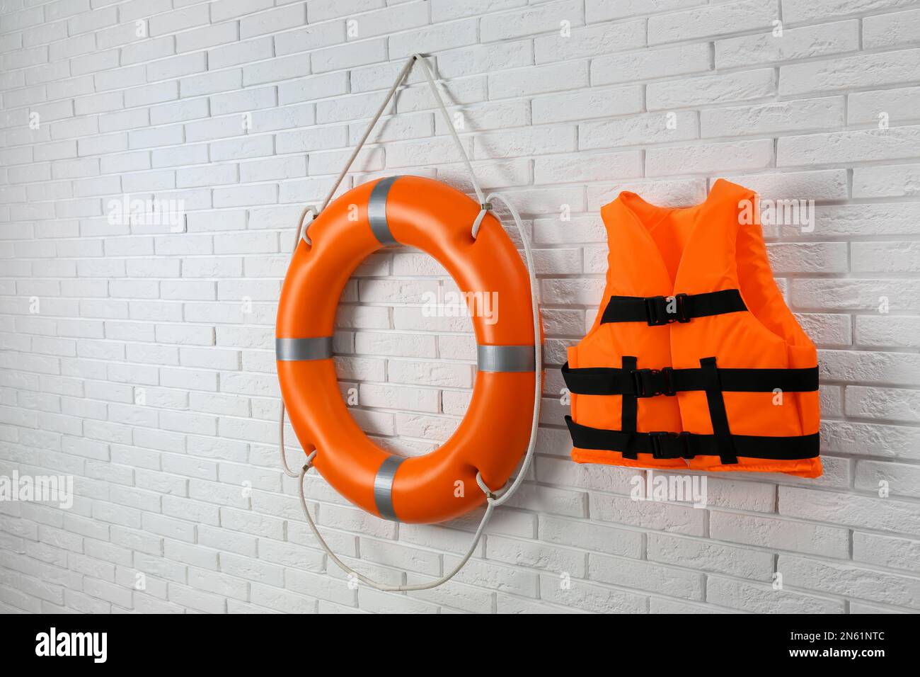 Orange life jacket and lifebuoy on white brick wall. Rescue equipment ...