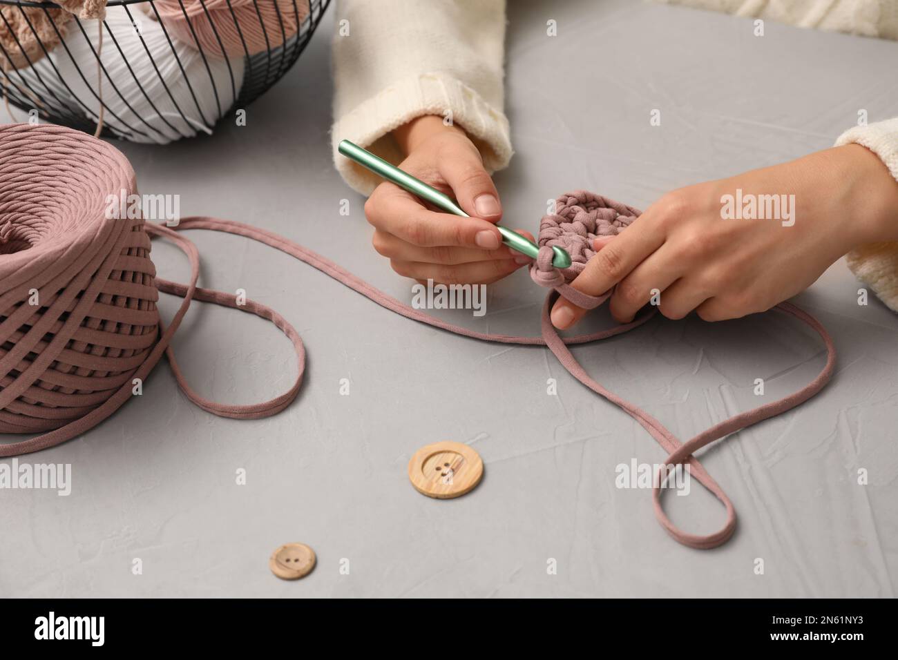 Woman crocheting with threads at grey table, closeup. Engaging hobby ...