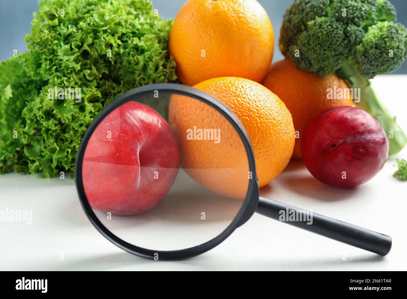 Fresh fruits, vegetables and magnifying glass on white table, closeup ...