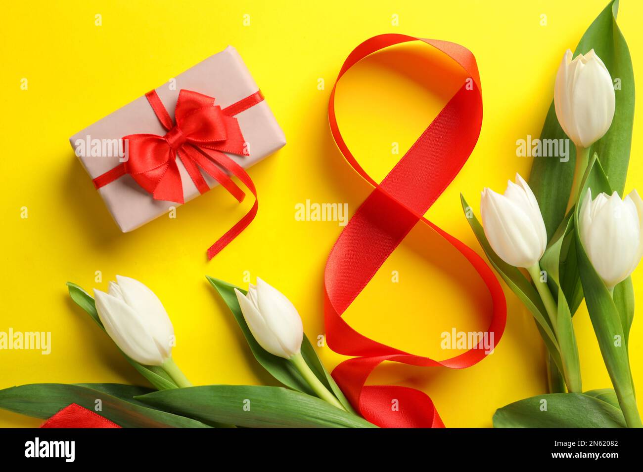 8 March card design with tulips and gift on yellow background, flat lay ...